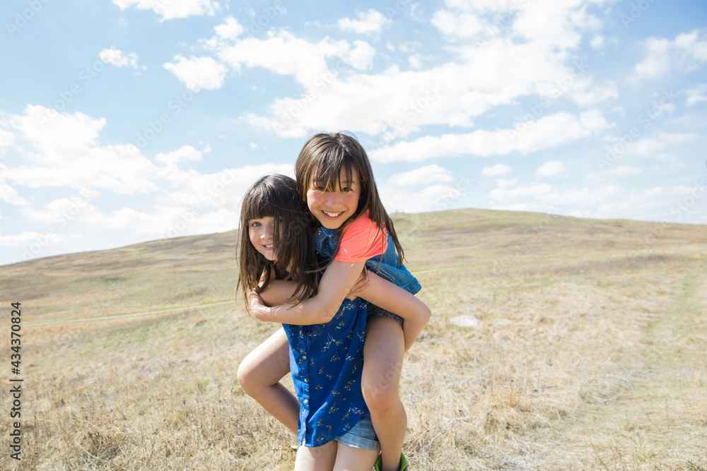 Portrait of little girl giving piggyback ride to friend on field Stock ...