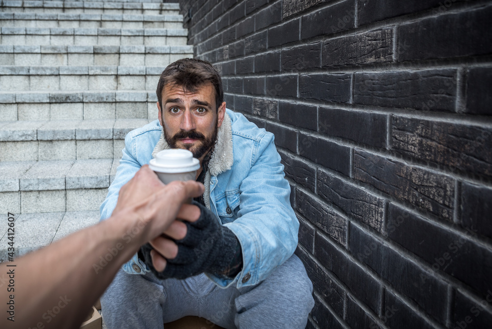 Hand giving a cup of coffee to young hungry homeless man sitting on the ...