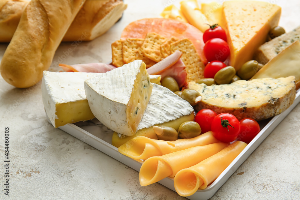 Tray with different types of cheese and snacks on light background ...