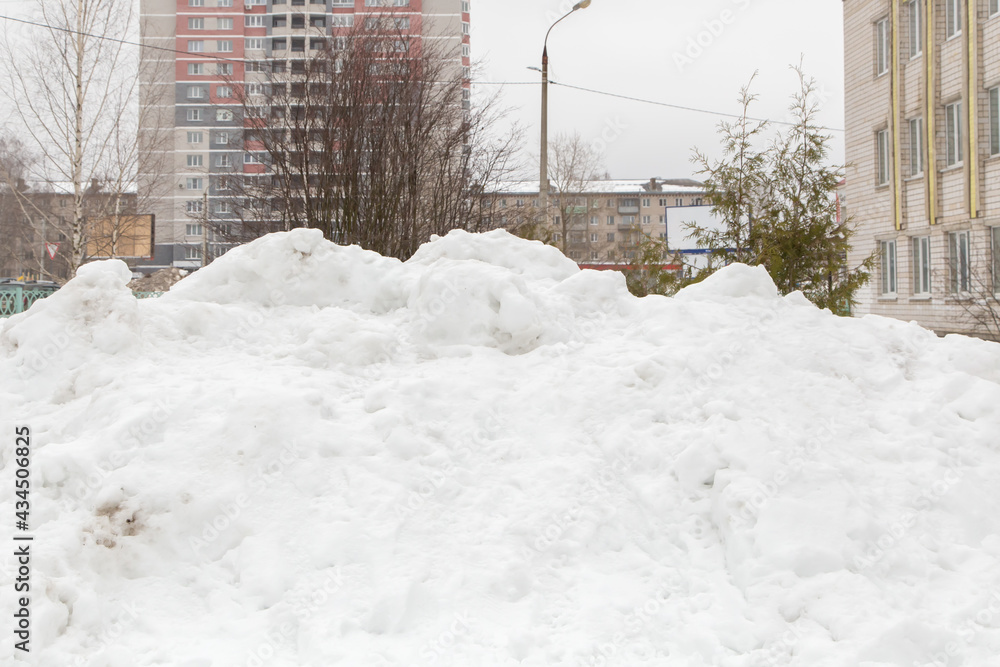 A large snowdrift on a city street with high-rise buildings. A block of ...