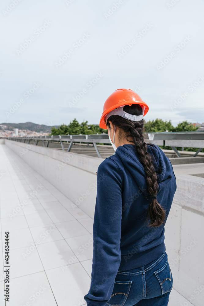 Young woman architect from behind with an orange helmet in a rooftop ...