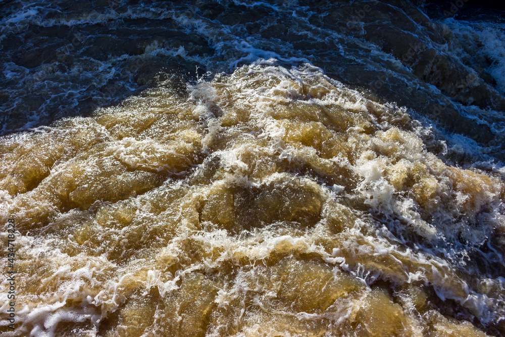 A stormy stream of water on a river dam, water with splashes and foam ...