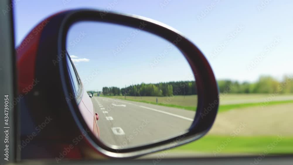 View in the rear view side mirror of a auto, driving a red car along ...
