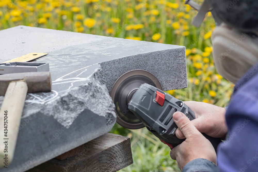 Street lighting. a masked worker processes a granite stone with a ...