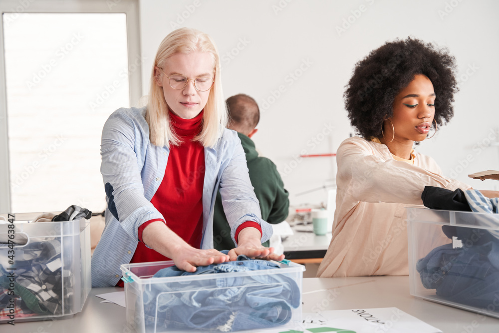 Worker putting jeans at the plastic box while sorting clothes for the ...