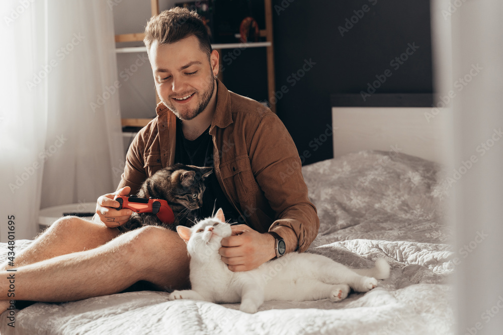 Man sitting at the bed with striped cat at the knees and stroking his ...