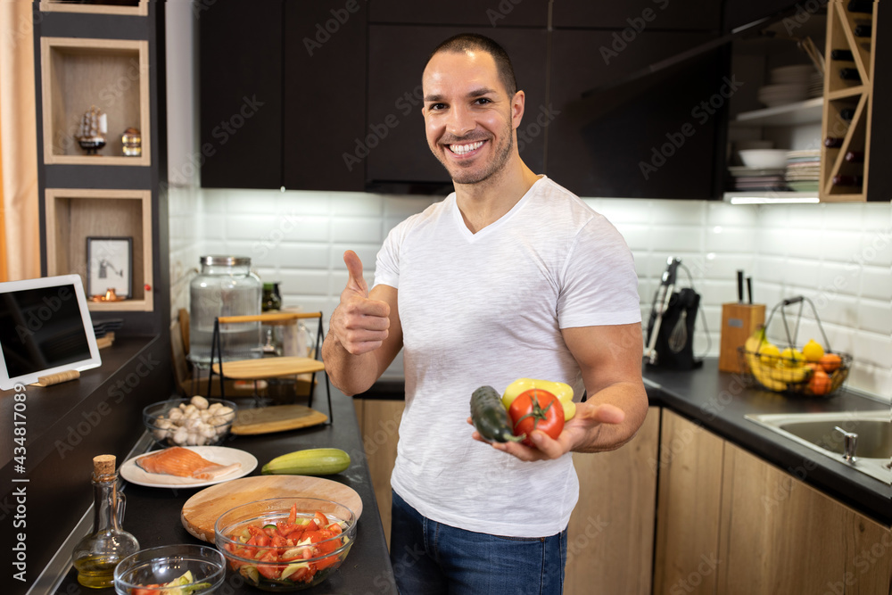 Muscular man holding thumbs up with one hand while holding vegetables ...