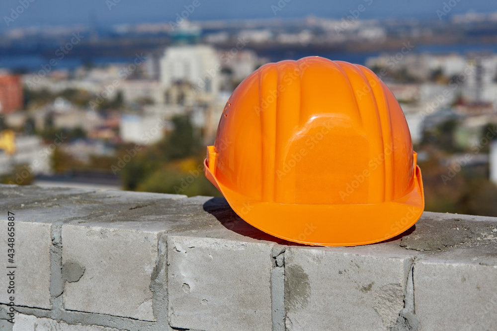 Orange plastic hard hat is on a brick wall. Roof of modern building ...