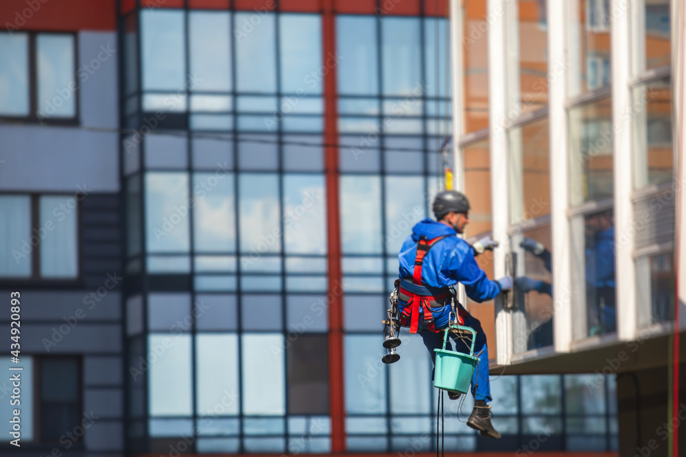 Professional climber rope access worker cleaning the windows on the ...