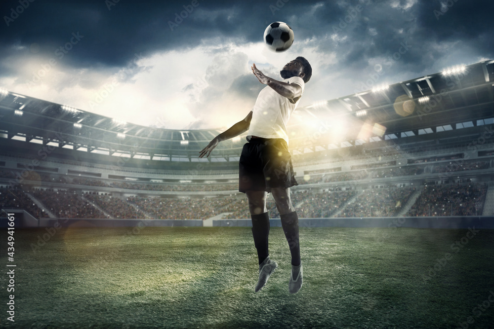 Professional male football, soccer player on stadium background. African fit athlete practicing ...