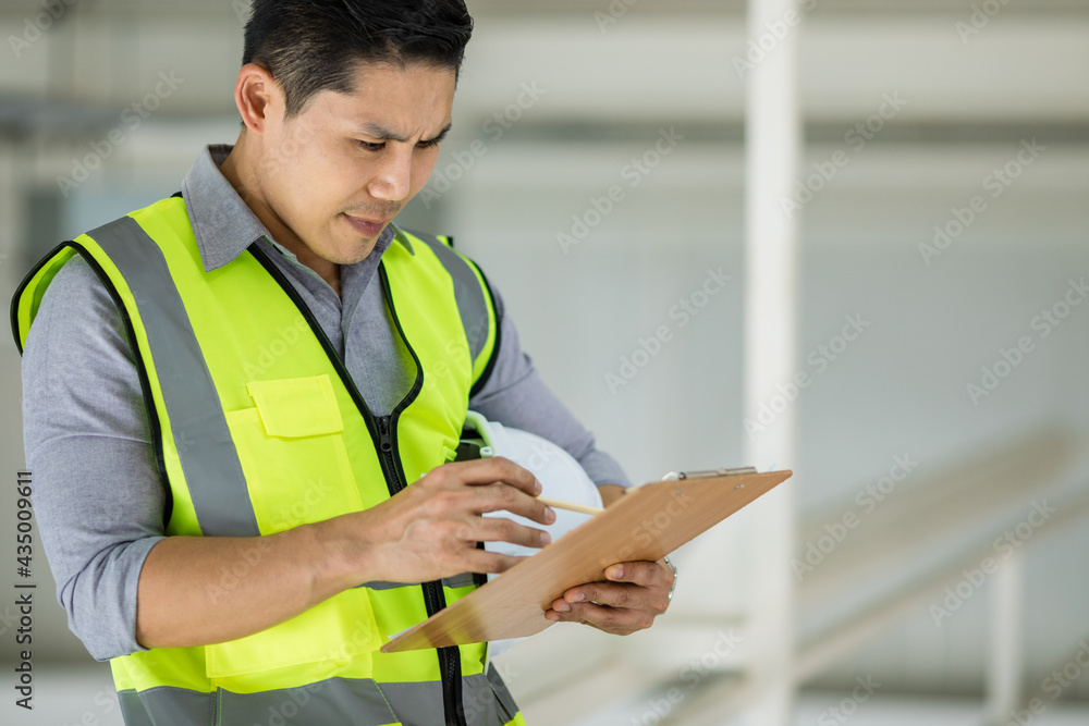 Handsome young Asian engineer in yellow reflective vest writing on ...