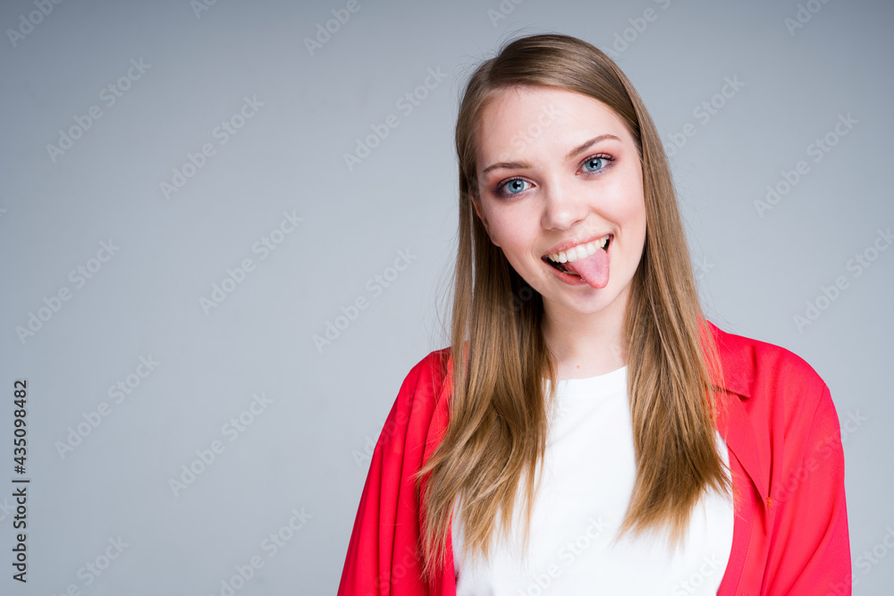 Cute cheerful girl smiles broadly and shows tongue at the camera while ...