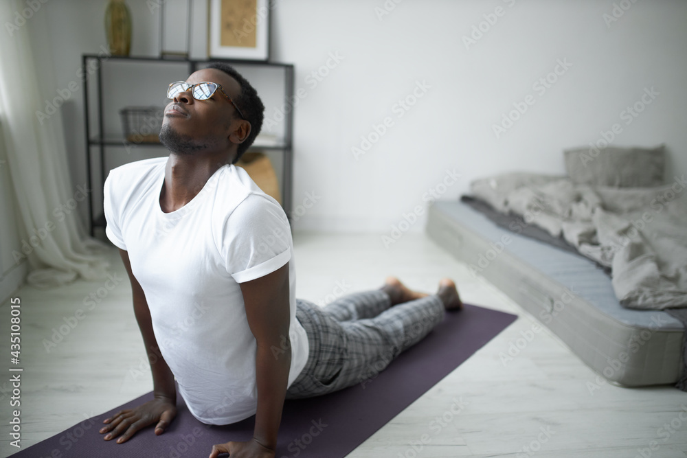 Active young Afro American man in glasses and comfy clothing exercising ...
