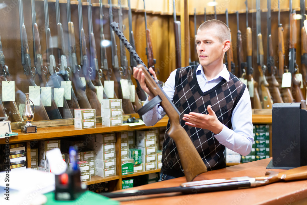 Confident seller of armory shop offering collection submachine gun with ...