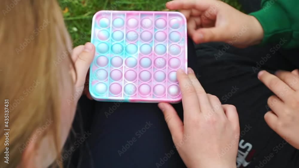 Boy and girl children playing colorful poppit sensory game. Close up of ...