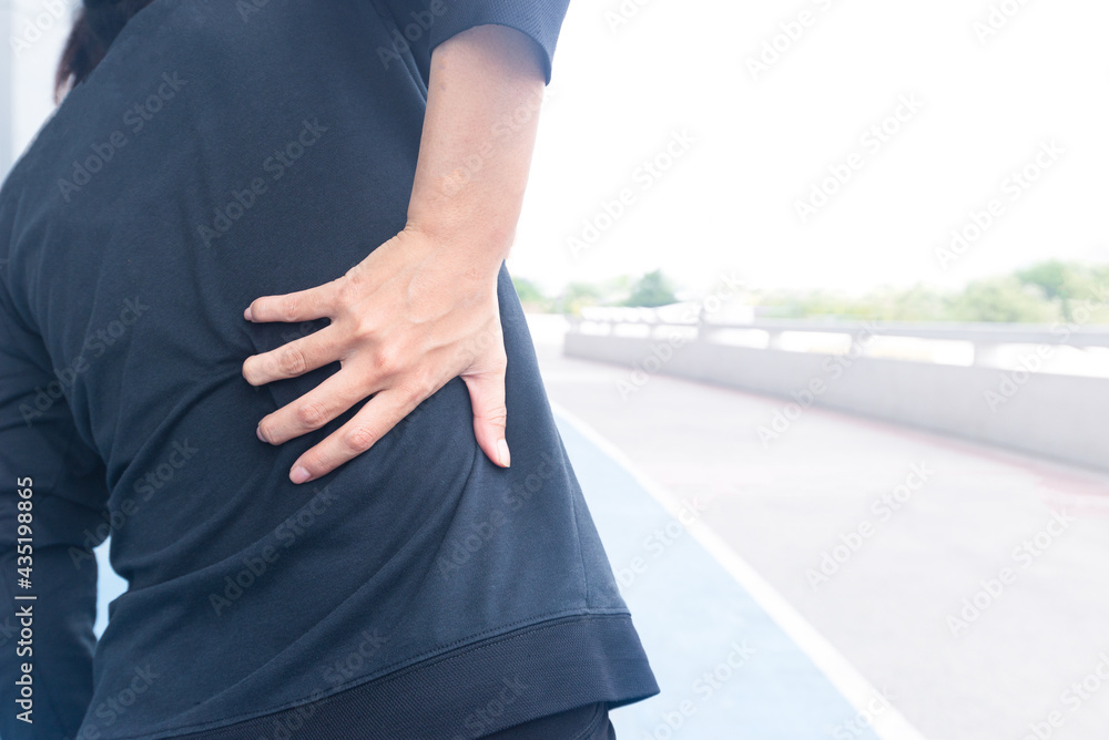 Woman athlete runner with back pain injury during training with hand ...