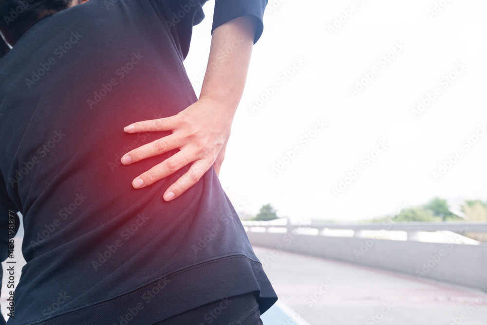 Woman athlete runner with back pain injury during training with hand ...