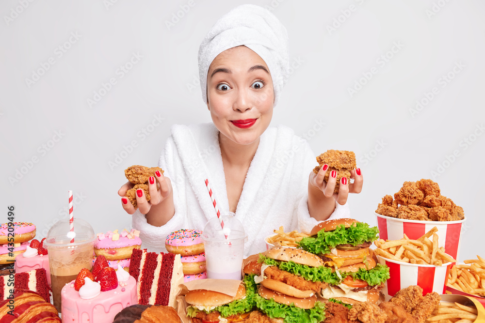 Surprised cheerful Asian woman focused at camera consumes too much fast ...