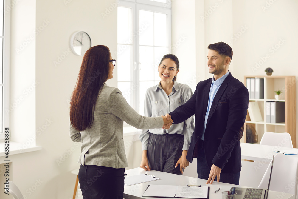 Office manager shaking hands with happy clients. Millennial couple ...