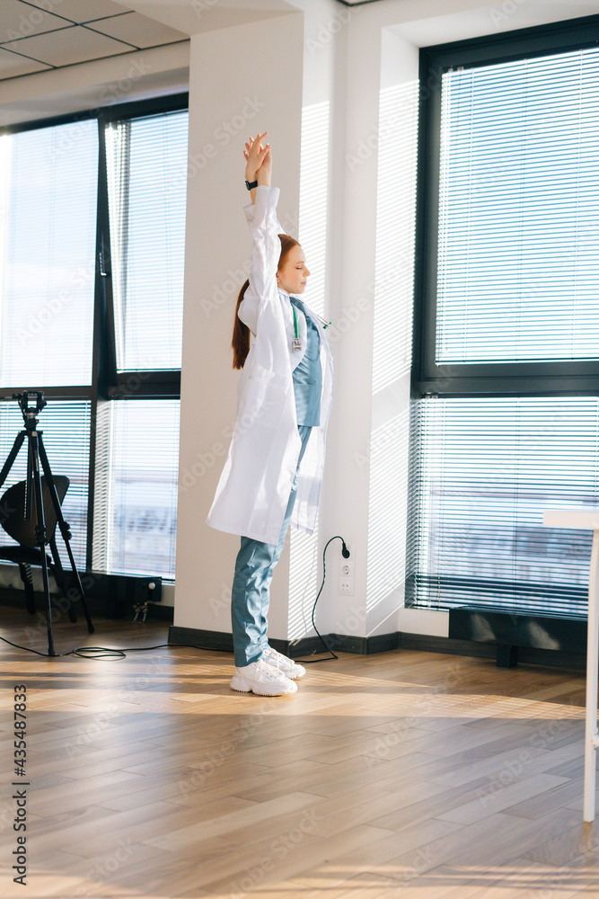 Side view of peaceful female doctor wearing white coat stretching hands ...