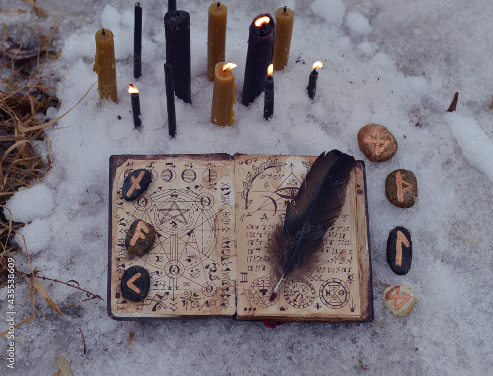 Top view of open witch book with spells, burning candles and runes ...