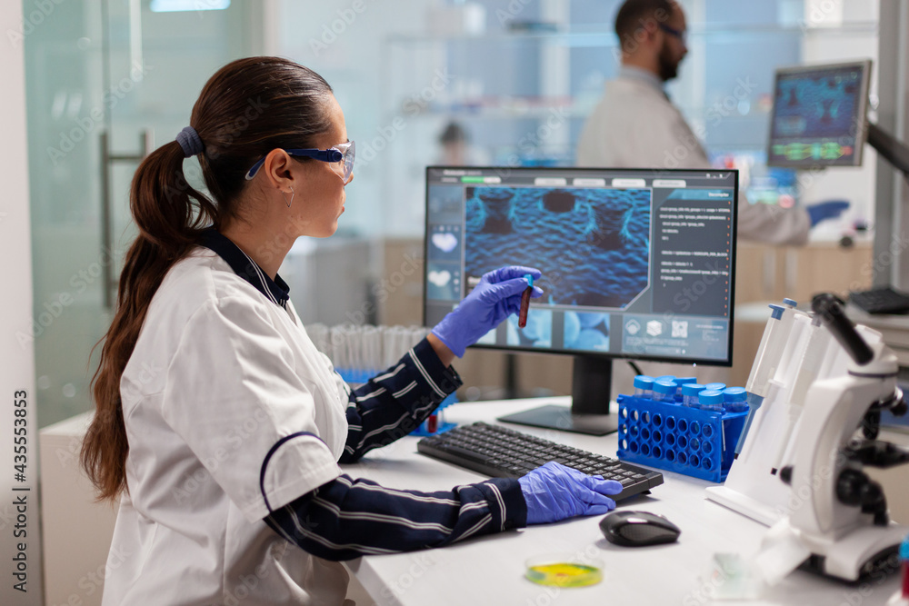 Medical researcher holding blood vaccutainer microbiology lab typing ...