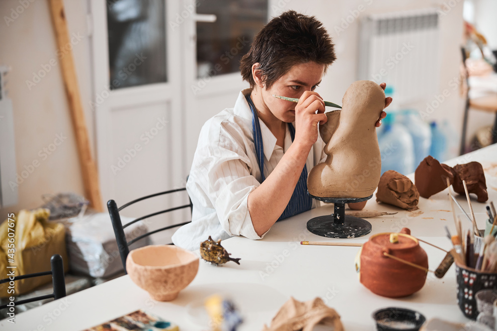 Accurate pottery shop employee shaping statue face with modeling knife ...