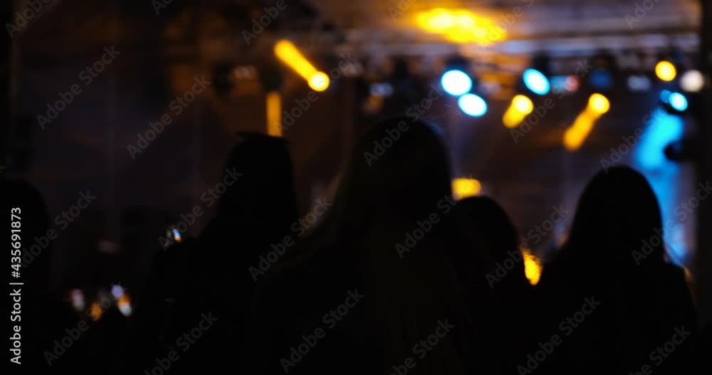 Cheering crowd in front of bright colorful stage lights. People are ...