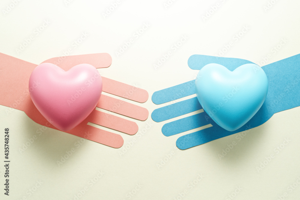 Concept image of gender equality. Pink hand holding pink heart and blue ...