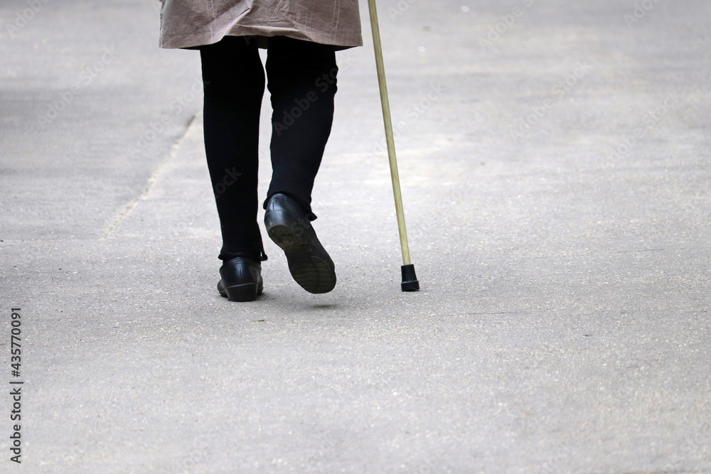 Woman walking with a cane on a street, female legs on sidewalk. Concept ...