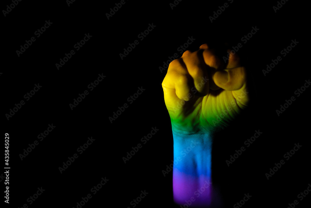 Raised fist illuminated with the LGBT pride flag on a black background ...