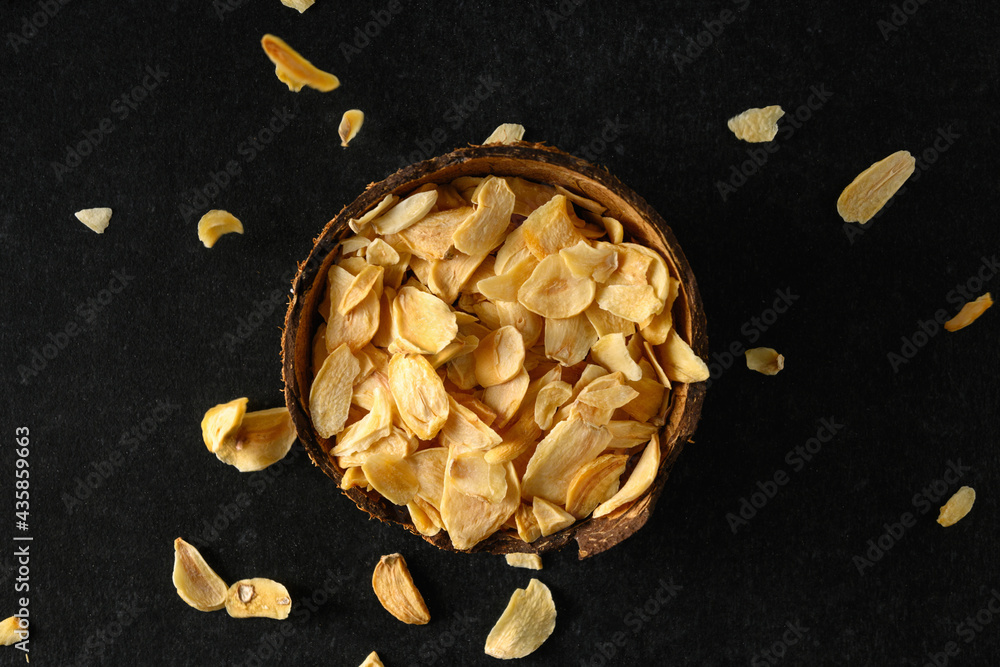 dry flakes of garlic in a coconut bowl, flakes falling from above on a ...