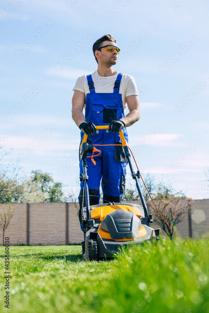 Young man mows the lawn using an electric lawn mower in a special ...