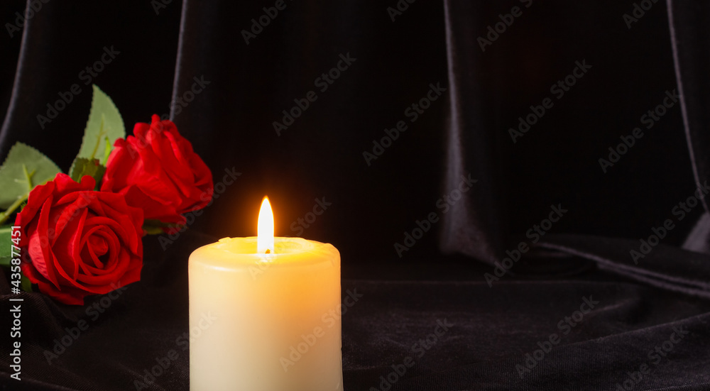 A burning candle and a red rose on a black background. The concept of ...