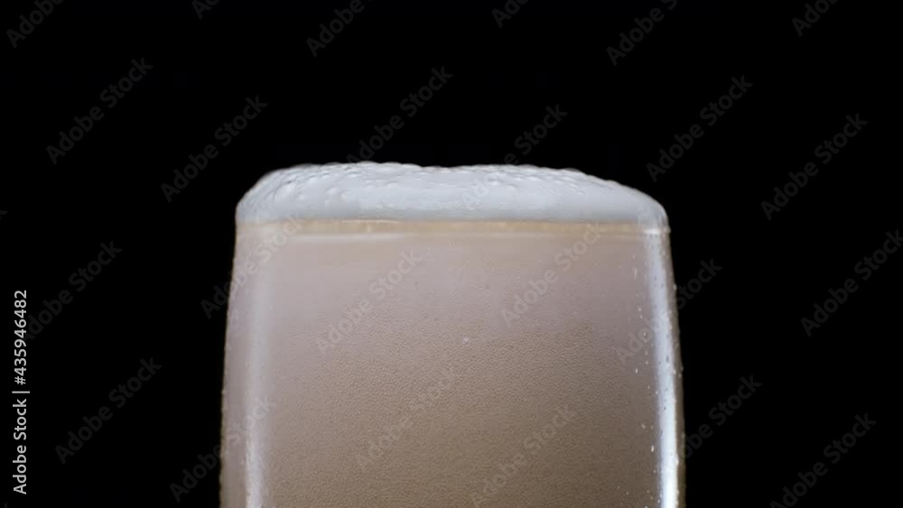 Pouring lager beer with bubbles and froth in glass over black ...