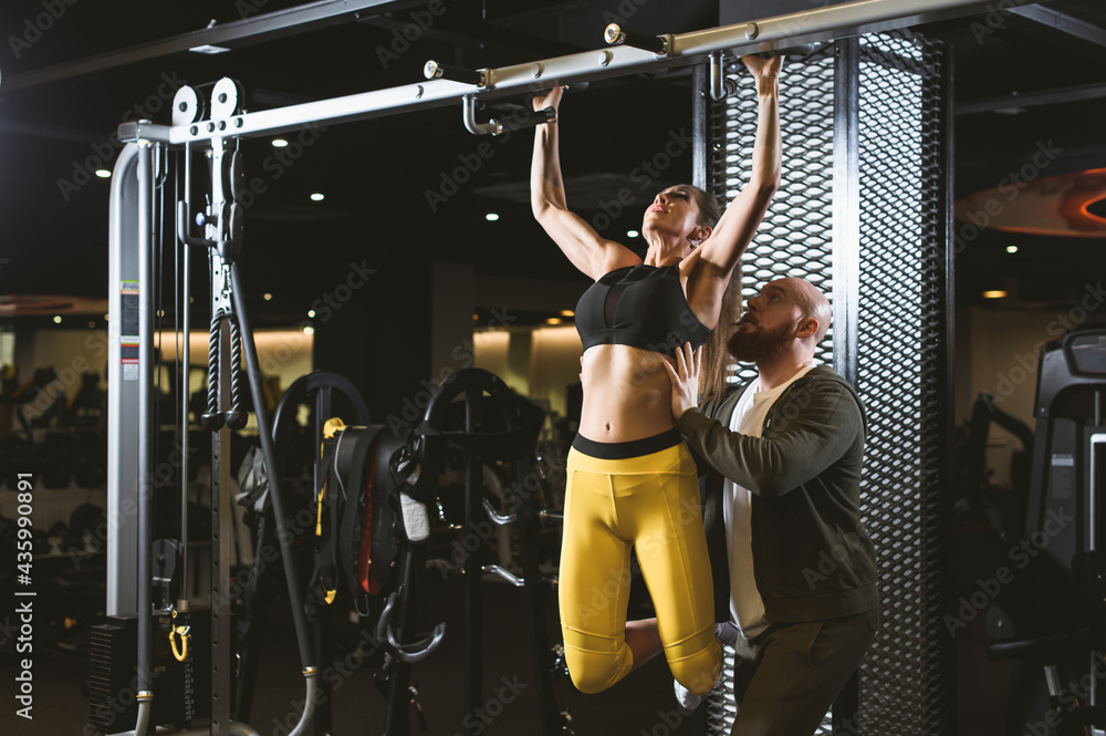 Muscular woman fitness model doing pull-ups. The coach looks after the ...
