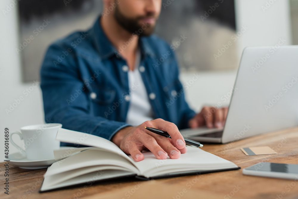 cropped view of teleworker working near notebook and laptop on blurred ...