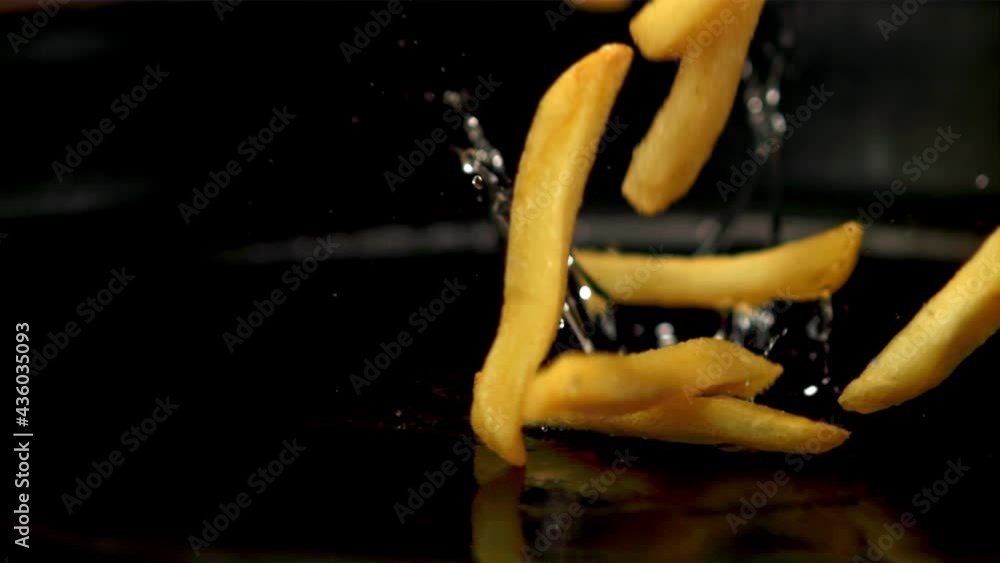 Super slow motion on a hot frying pan drops french fries. On a black ...