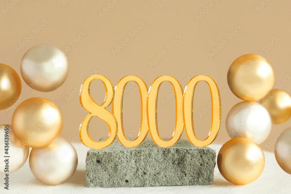 Number 8000 on a concrete podium and volumetric golden balls on a beige ...
