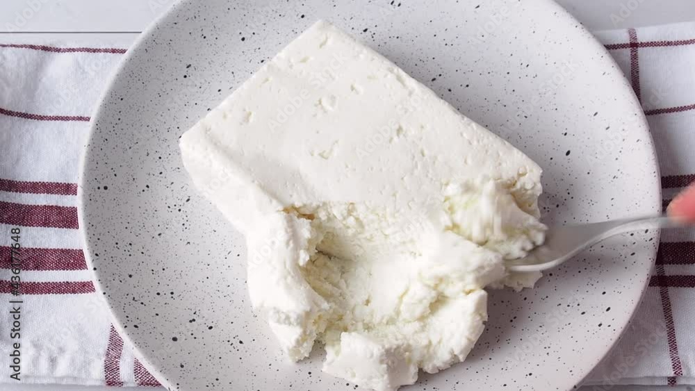 Soft cottage cheese curd is kneaded with a fork in a plate. Fermented ...