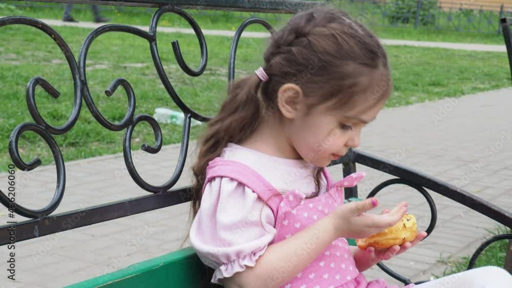 Vidéo Stock girl on a park bench eating a donut with yellow frosting ...