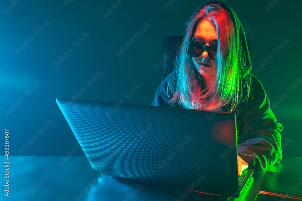 Woman hacker next to a laptop. Girl hacker in the neon light. Hacking. Woman cracker works in ...
