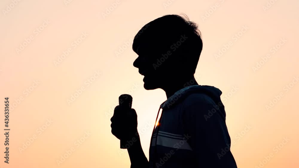 Silhouette of a kid screaming in the mic in front of the sun during the ...