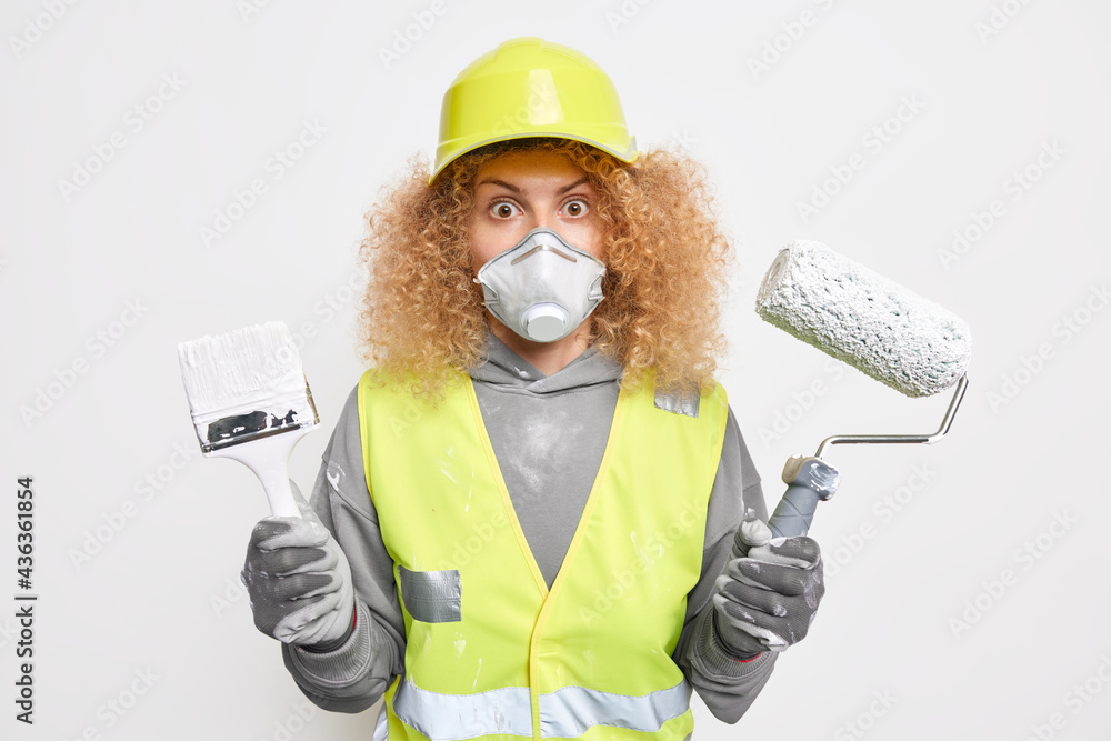 Photo of stunned curly female engineer holds painting roller and brush ...