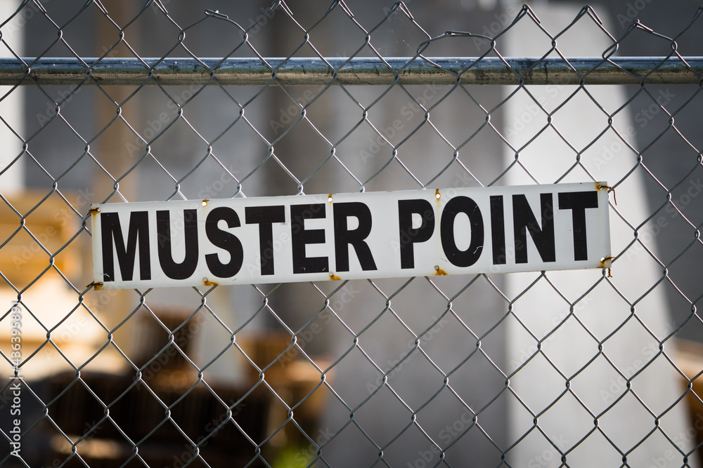 Muster point sign posted on a construction site chain link fence. Fire ...