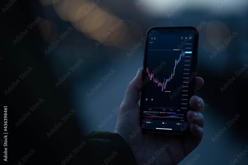 Trader holding smartphone with financial chart and analyzing price flow ...