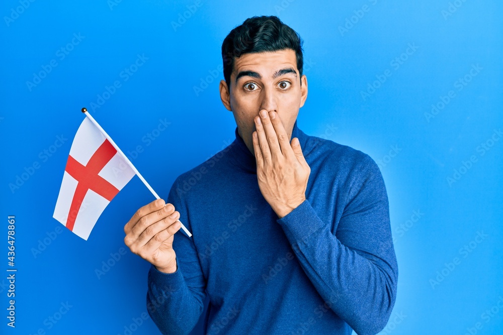 Handsome hispanic man holding england flag covering mouth with hand ...