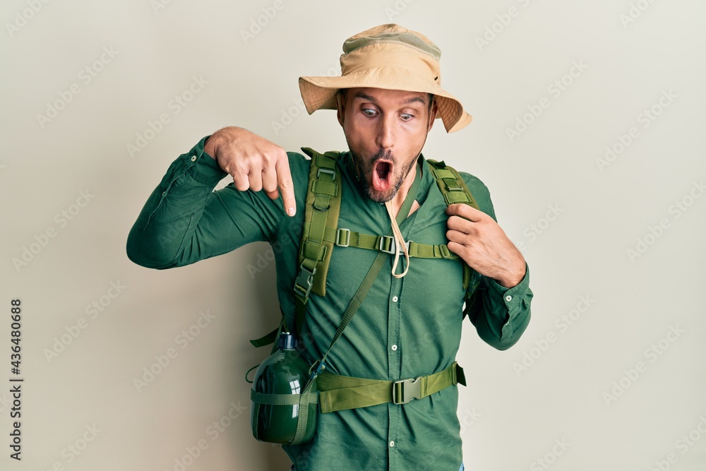 Handsome man with beard wearing explorer hat and backpack pointing down ...
