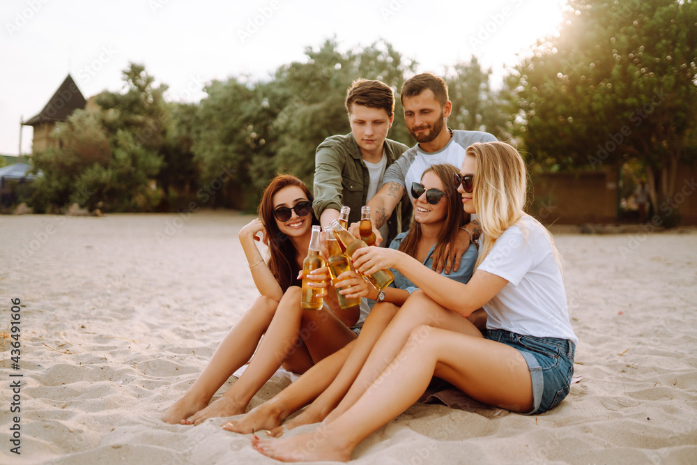 Group of friends cheers and drink beers on the beach. Young friends ...