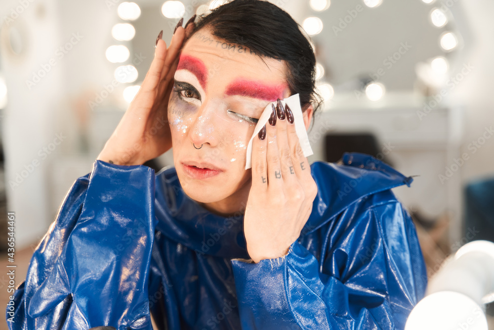 Drag queen remove his vivid makeup while sitting in front of the mirror ...